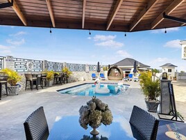 Uma área de piscina coberta ao ar livre, com teto de madeira, espreguiçadeiras e uma mesa com um arranjo floral.