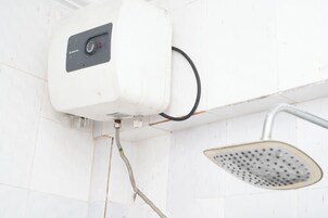 Chuveiro fixado em parede revestida de azulejos brancos, com painel de controle.