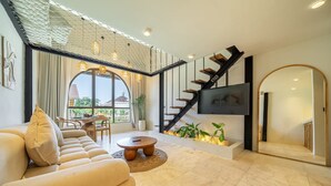 Uma sala de estar moderna com sofá, mesa de centro, escada, televisão e janelas amplas.