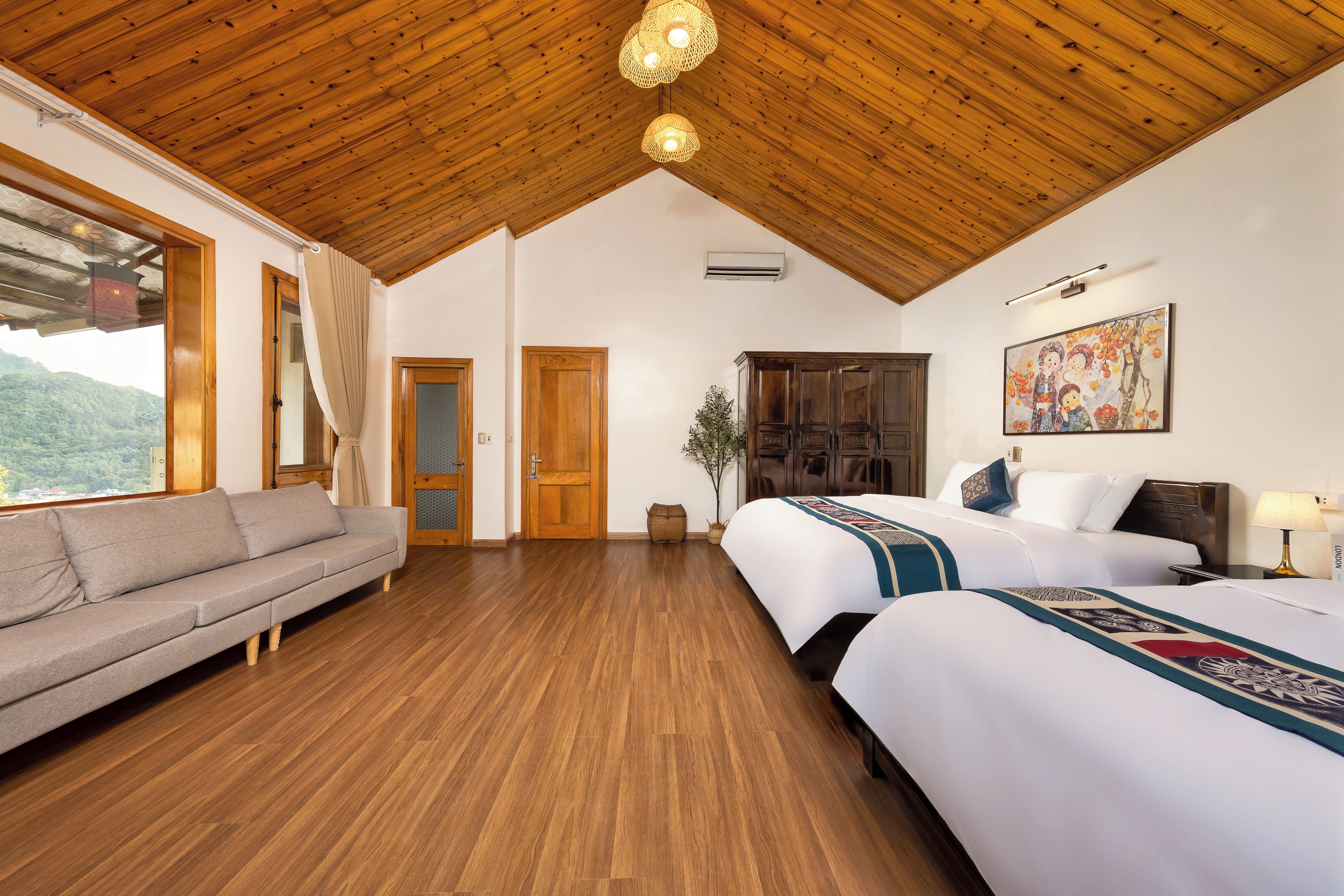 Quarto de hotel com teto de madeira, sofá, cama com colcha estampada, quadro na parede e vista para o exterior.