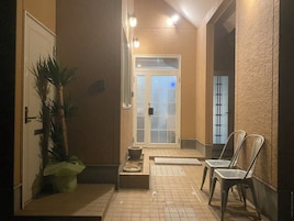 Um corredor com uma porta que dá para um quarto, uma planta em vaso e duas cadeiras.