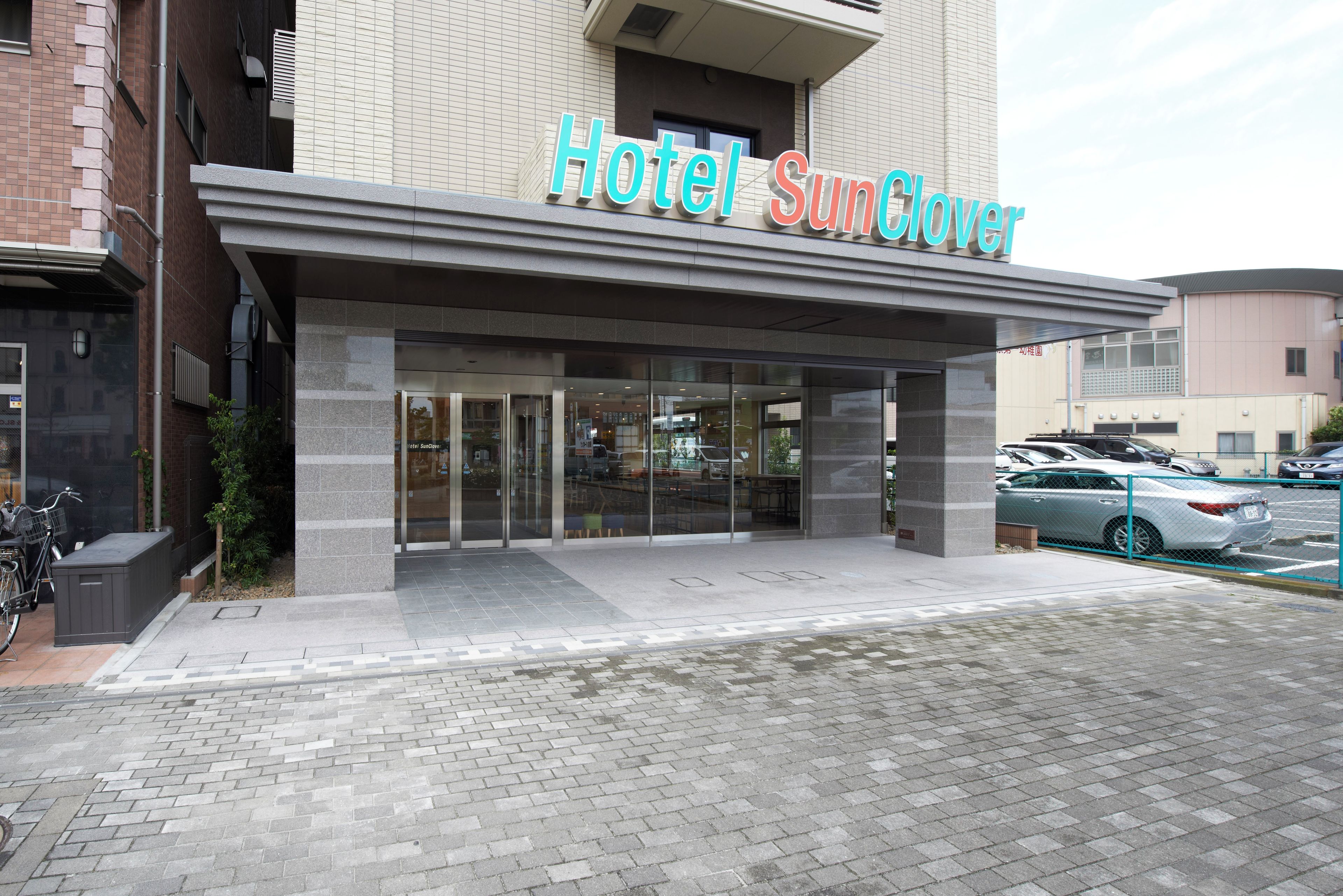 Entrada de hotel com design moderno, apresentando uma placa chamativa com a inscrição 'Hotel Sunflower'.