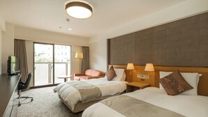 Quarto de hotel com duas camas, uma escrivaninha, uma cadeira, uma mesinha e vista para o exterior.