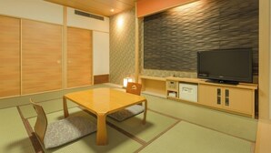 Um quarto japonês tradicional com tatames, uma mesa baixa, uma televisão sobre um móvel e portas corrediças.