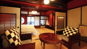 Um quarto tradicional japonês com tatames, uma mesa baixa e uma cama com cabeceira vermelha.