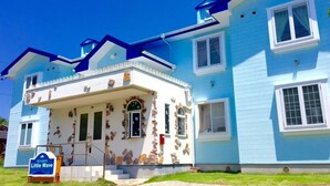 Uma casa de dois andares com fachada azul, varanda frontal e uma placa indicando 'Little Wave'.