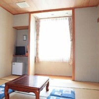 Um quarto com piso de tatame, uma mesa de madeira, uma televisão em uma estante e uma janela com cortinas.