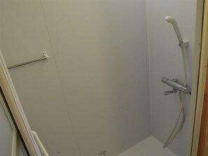 Um chuveiro pequeno e fechado, com um chuveiro manual e um porta-toalhas.