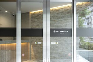 Interior moderno com balcão de recepção, parede com textura de pedra e porta de vidro com placa de 'Proibida a Entrada'.