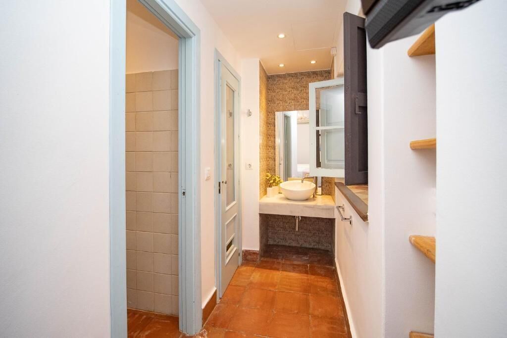 Um corredor estreito com um banheiro que tem uma pia branca, um espelho e um revestimento de azulejos.