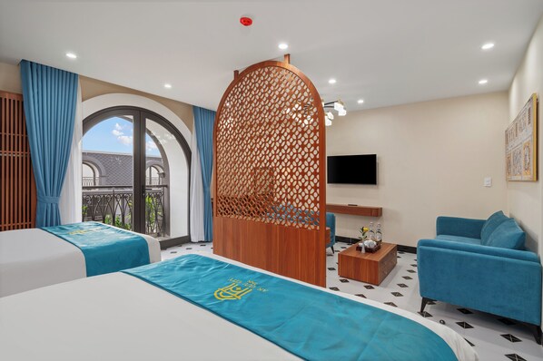 Quarto de hotel com duas camas, um sofá, uma TV e uma varanda com cortinas azuis.