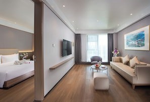 Quarto de hotel com cama, sofá, televisão, mesa de centro e um quadro na parede.
