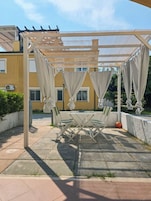 Um pátio externo com pérgola, mesa e cadeiras.