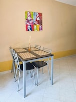 Uma sala de jantar com uma mesa e cadeiras, um vaso com gravetos e uma obra de arte colorida na parede.