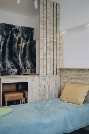 Quarto com cama, escrivaninha e TV fixada na parede.