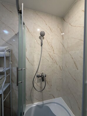 Um banheiro com chuveiro, área de banho com divisória de vidro, banheira branca e porta-toalhas com toalhas.