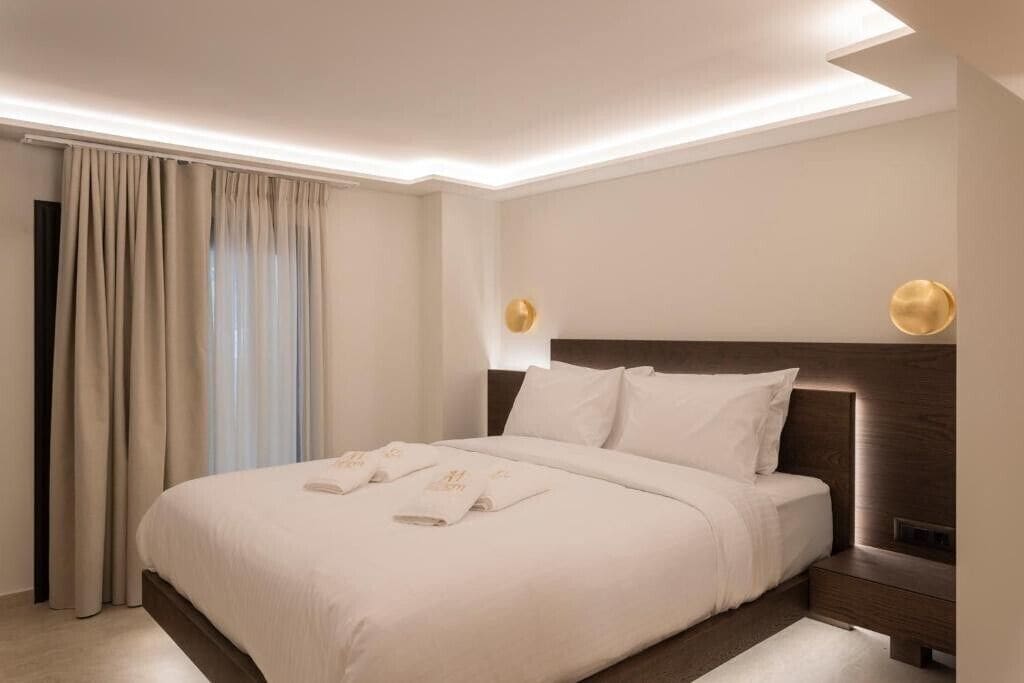 Quarto de hotel moderno com uma cama grande, uma mesinha de cabeceira e um candeeiro fixado na parede.