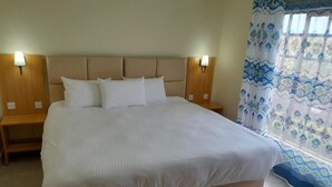 Uma cama grande com cabeceira, duas mesas de cabeceira e uma janela com cortinas estampadas.