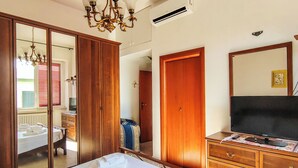 Quarto de hotel com cama, cómoda, televisão, guarda-roupa e um candelabro.