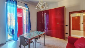 Uma área de refeições com mesa e cadeiras, um sofá vermelho, um candelabro e portas vermelhas.