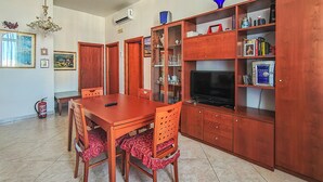 Uma sala de jantar com mesa e cadeiras de madeira, televisão e estante de livros.