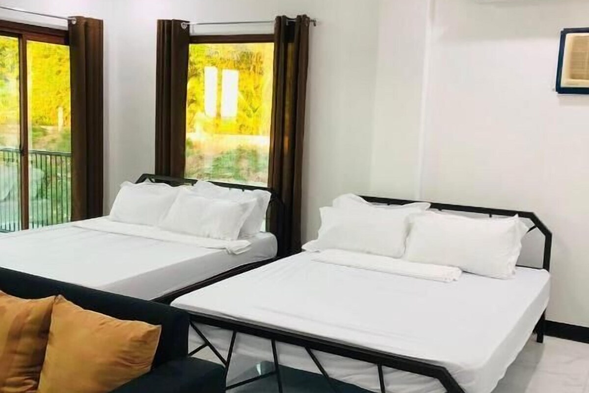 Quarto com duas camas, um sofá preto e uma janela com cortinas.