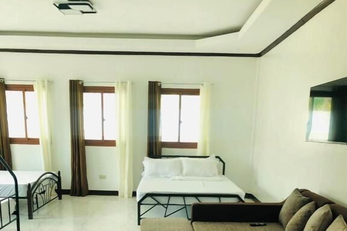 Quarto de hotel com cama, sofá, mesa de jantar e janela com cortinas.