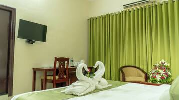 Quarto de hotel com cama, escrivaninha, cadeira, televisão e cortina verde.