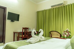 Quarto de hotel com cama, escrivaninha, cadeira, televisão e cortina verde.