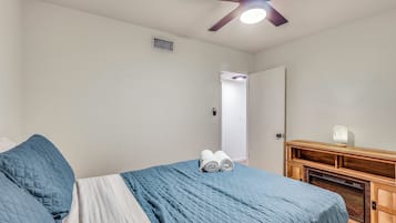 Um quarto com cama, ventilador de teto, cômoda de madeira e porta que dá para outro espaço.