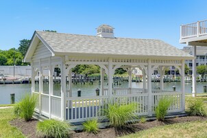 Um gazebo branco com teto pontiagudo, cercado por água e vegetação.