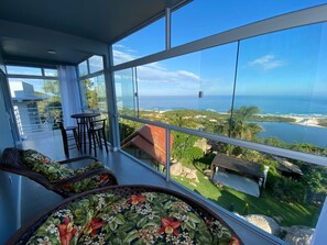 Varanda com vista para o oceano, móveis de vime e parede de vidro.