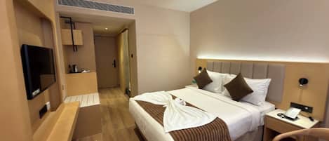 Quarto de hotel com cama, mesa de cabeceira, cadeira, televisão e uma pequena mesa com flores.