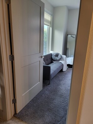 Um quarto com uma cama, um sofá cinzento, uma janela e uma porta.