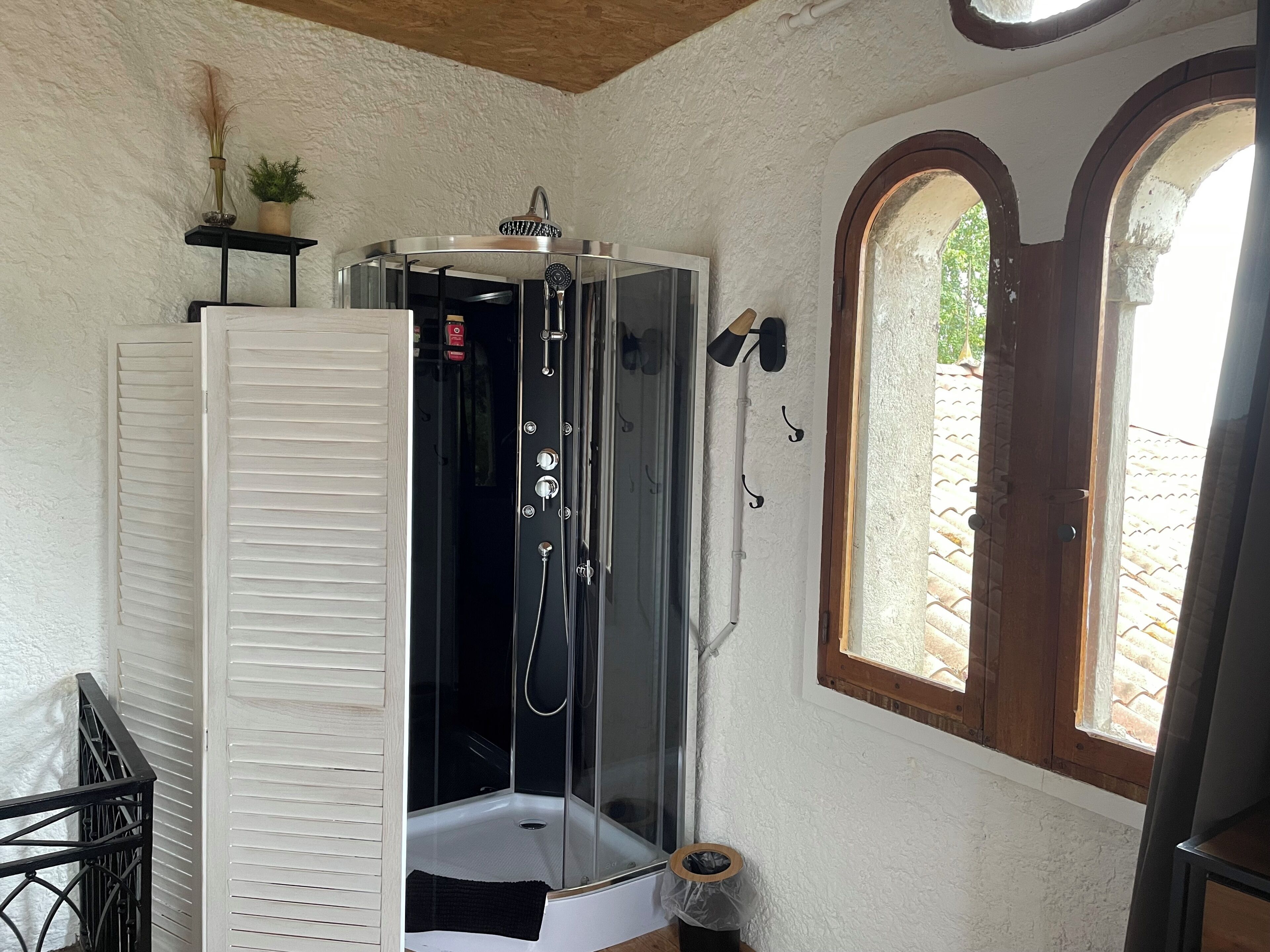 Casa de banho com cabine de duche de vidro, porta branca e janela com moldura de madeira.