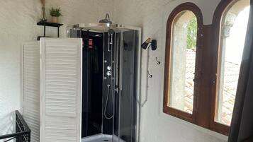 Casa de banho com cabine de duche de vidro, porta branca e janela com moldura de madeira.