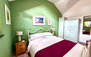 Quarto com cama, duas mesas de cabeceira, um guarda-roupa e duas fotografias emolduradas na parede.