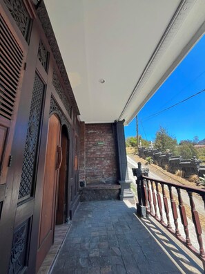 Um espaço ao ar livre coberto, com piso de pedra, porta de madeira e corrimão de metal.
