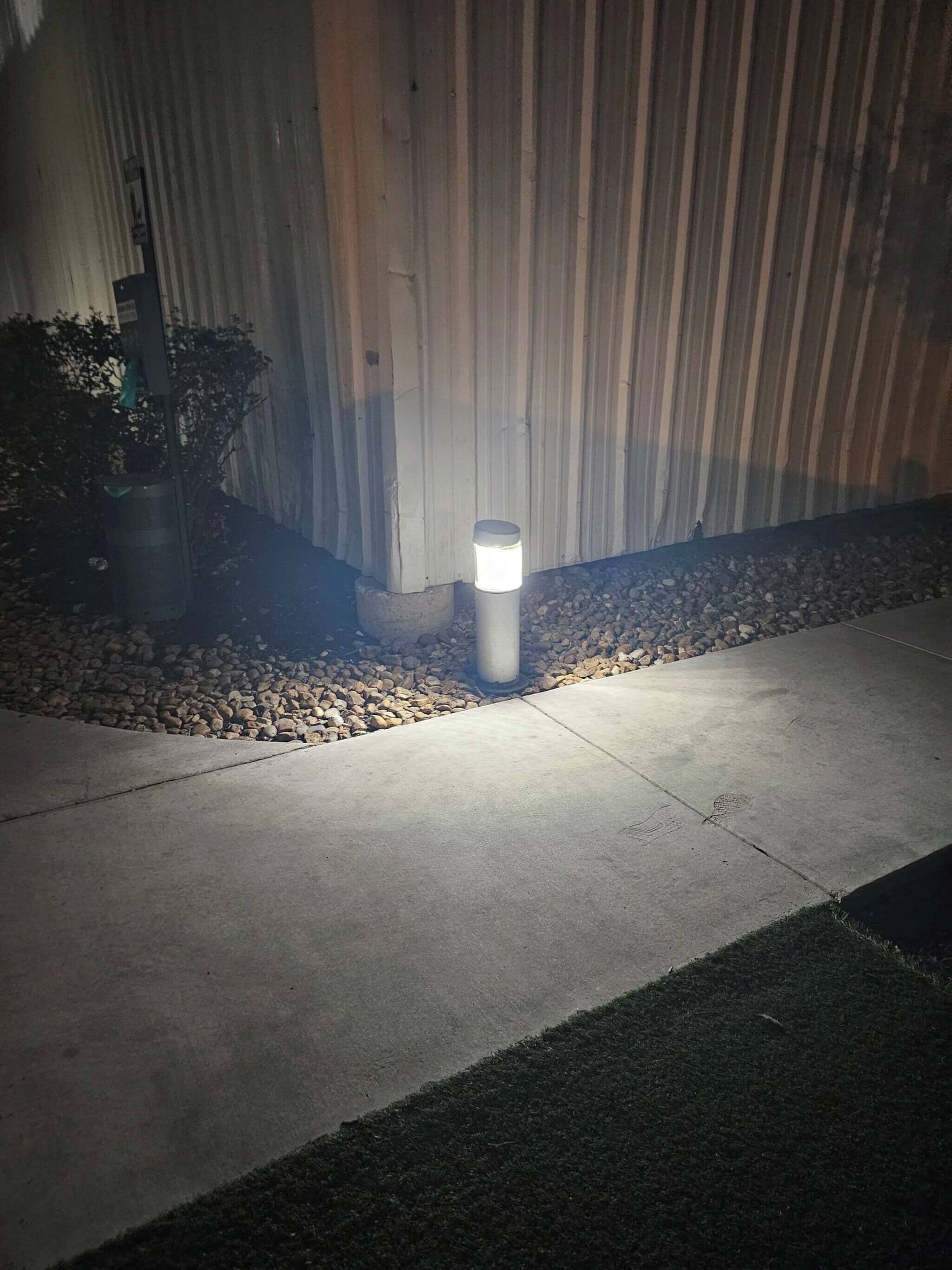 Um caminho que leva a um edifício com um poste de luz e um vaso de planta.