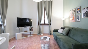 Uma sala de estar com televisão de tela plana em um suporte, um sofá verde, uma mesa de centro e um abajur.