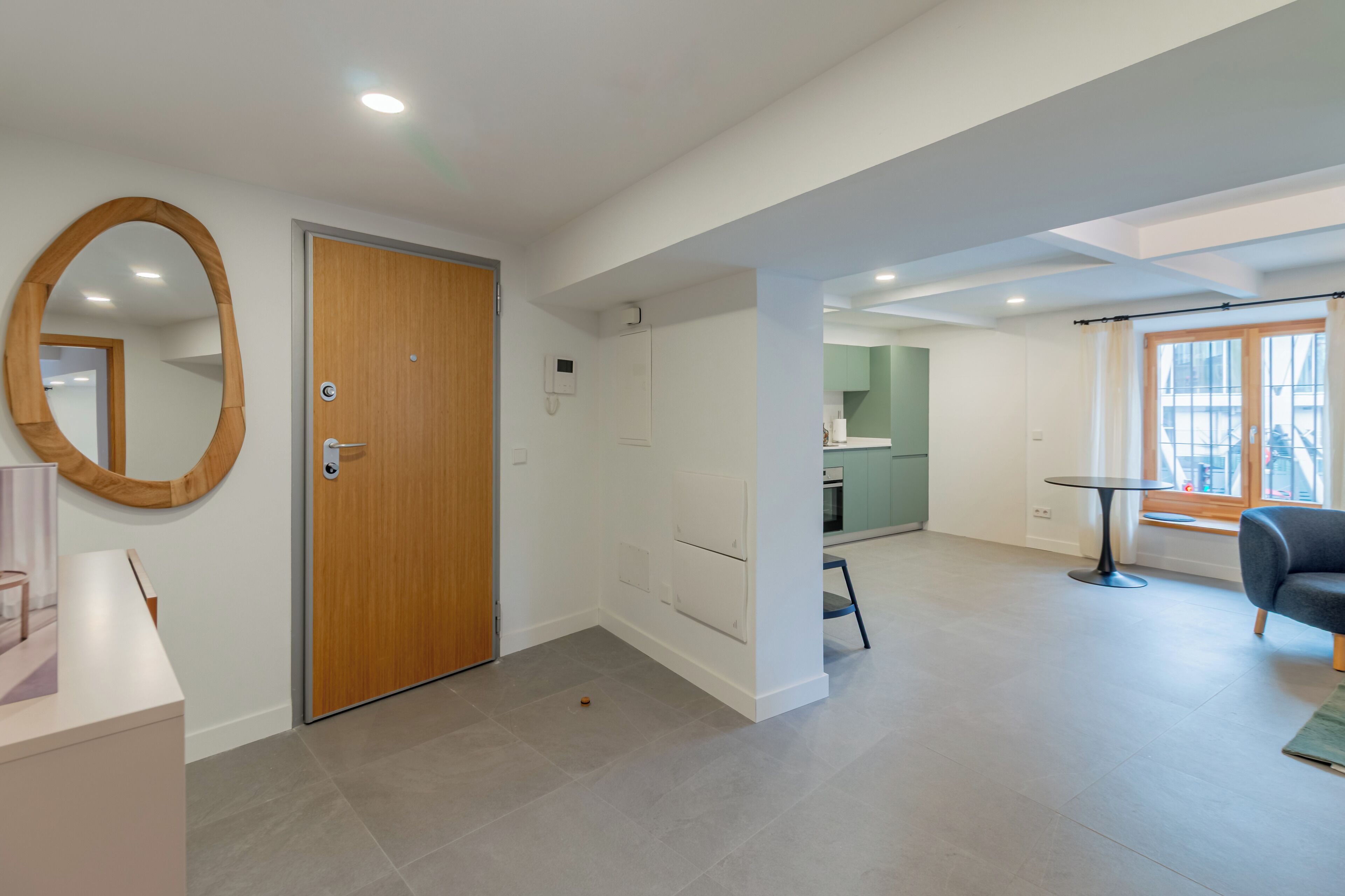 Um quarto espaçoso com porta de madeira, um espelho redondo, uma mesa pequena e uma cadeira.