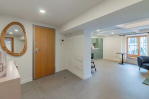 Um quarto espaçoso com porta de madeira, um espelho redondo, uma mesa pequena e uma cadeira.