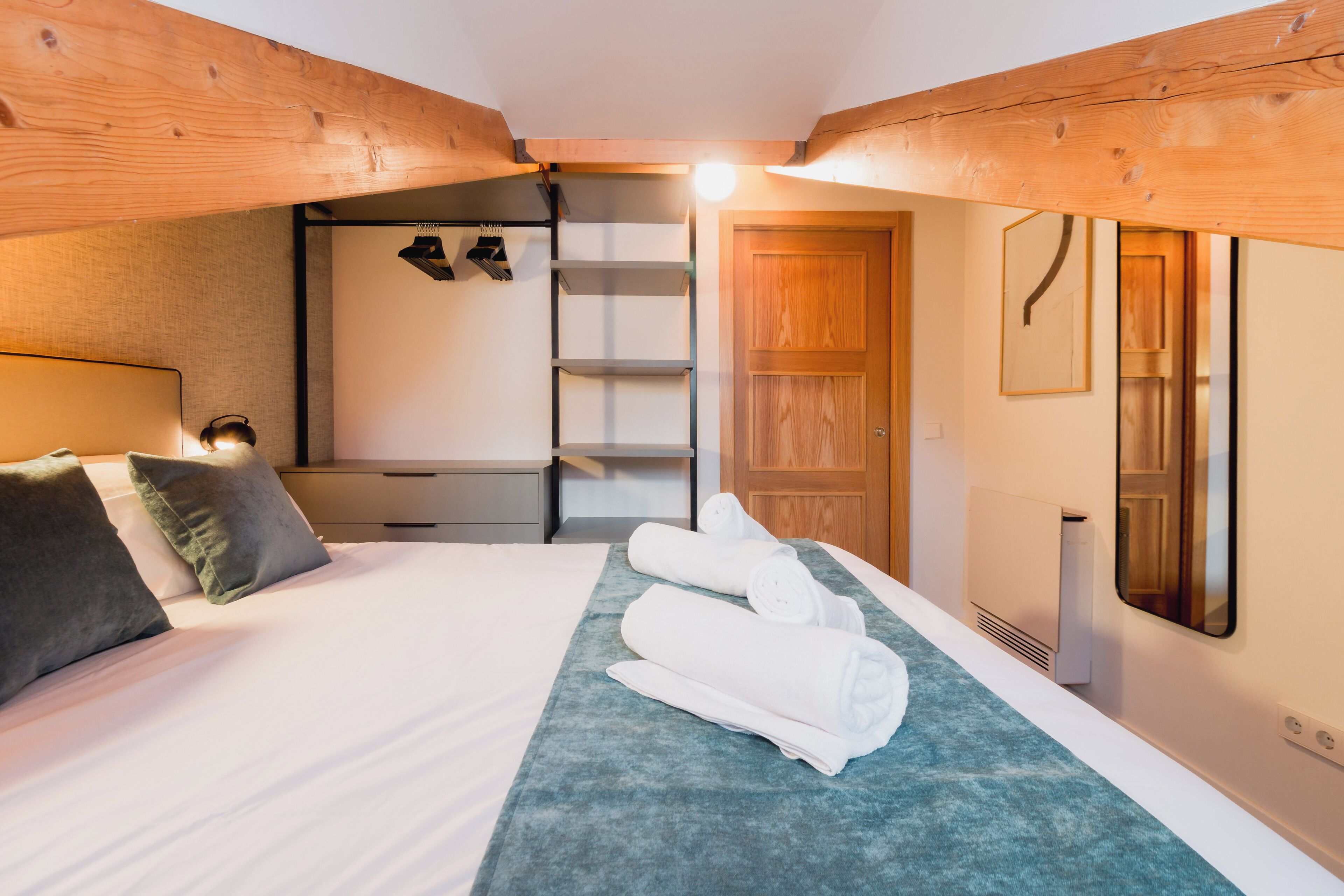 Quarto de hotel com cama, mesa de cabeceira, prateleira na parede, guarda-roupa e espelho.