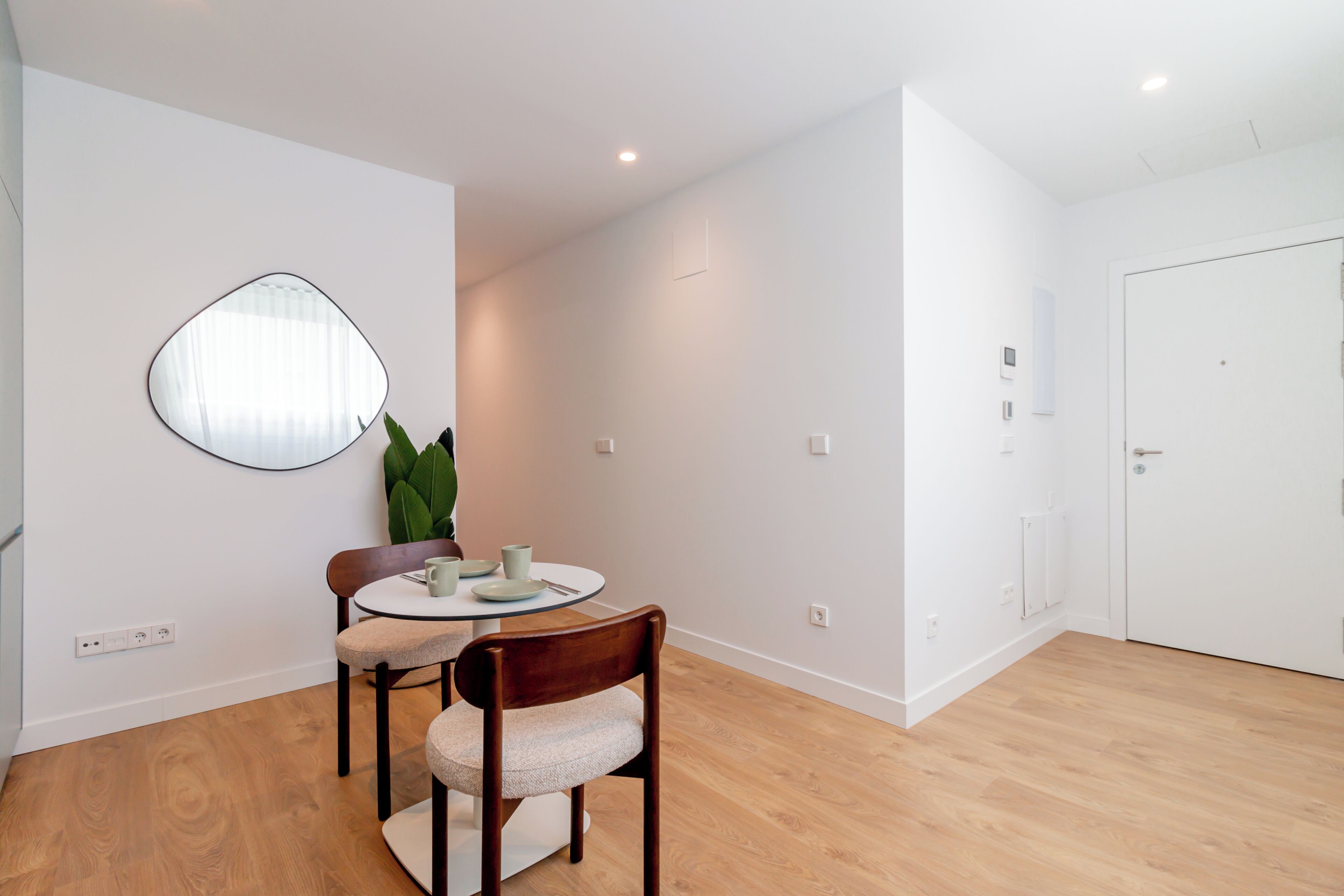 Quarto moderno com mesa de jantar redonda, duas cadeiras, um espelho e um vaso de planta.