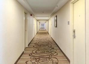 Um corredor de hotel com piso coberto de carpete, portas em ambos os lados e luminária no teto.