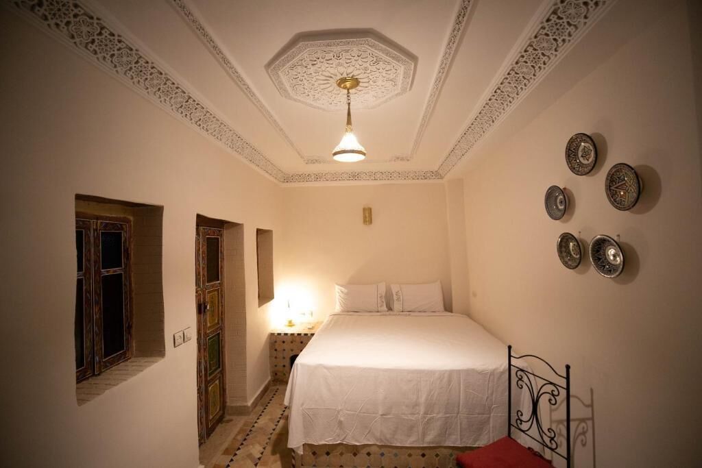 Quarto com cama, mesa de cabeceira, luminária na parede e pratos decorativos.