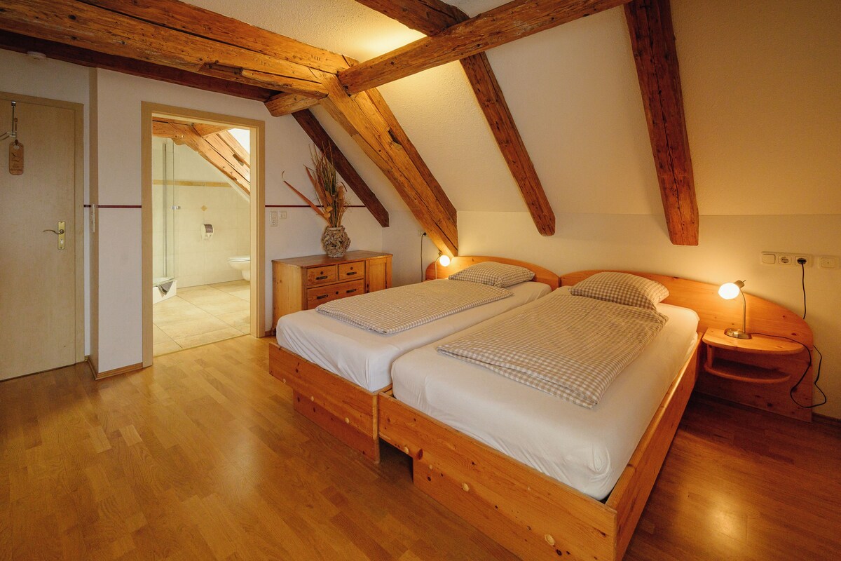 Quarto com cama de madeira, mesa de cabeceira com abajur e cômoda de madeira.