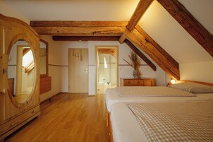 Quarto com teto inclinado, vigas de madeira, espelho grande, cama com roupa de cama xadrez e mesa de cabeceira com luminária.