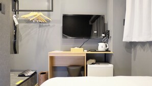 Quarto de hotel com cama, secretária com chaleira, televisão e cabideiro.