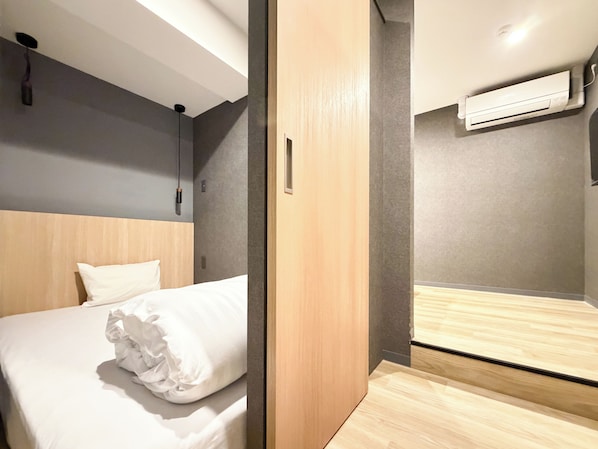 Quarto de hotel com cama, cabeceira de madeira, ar condicionado fixado na parede e piso de madeira.